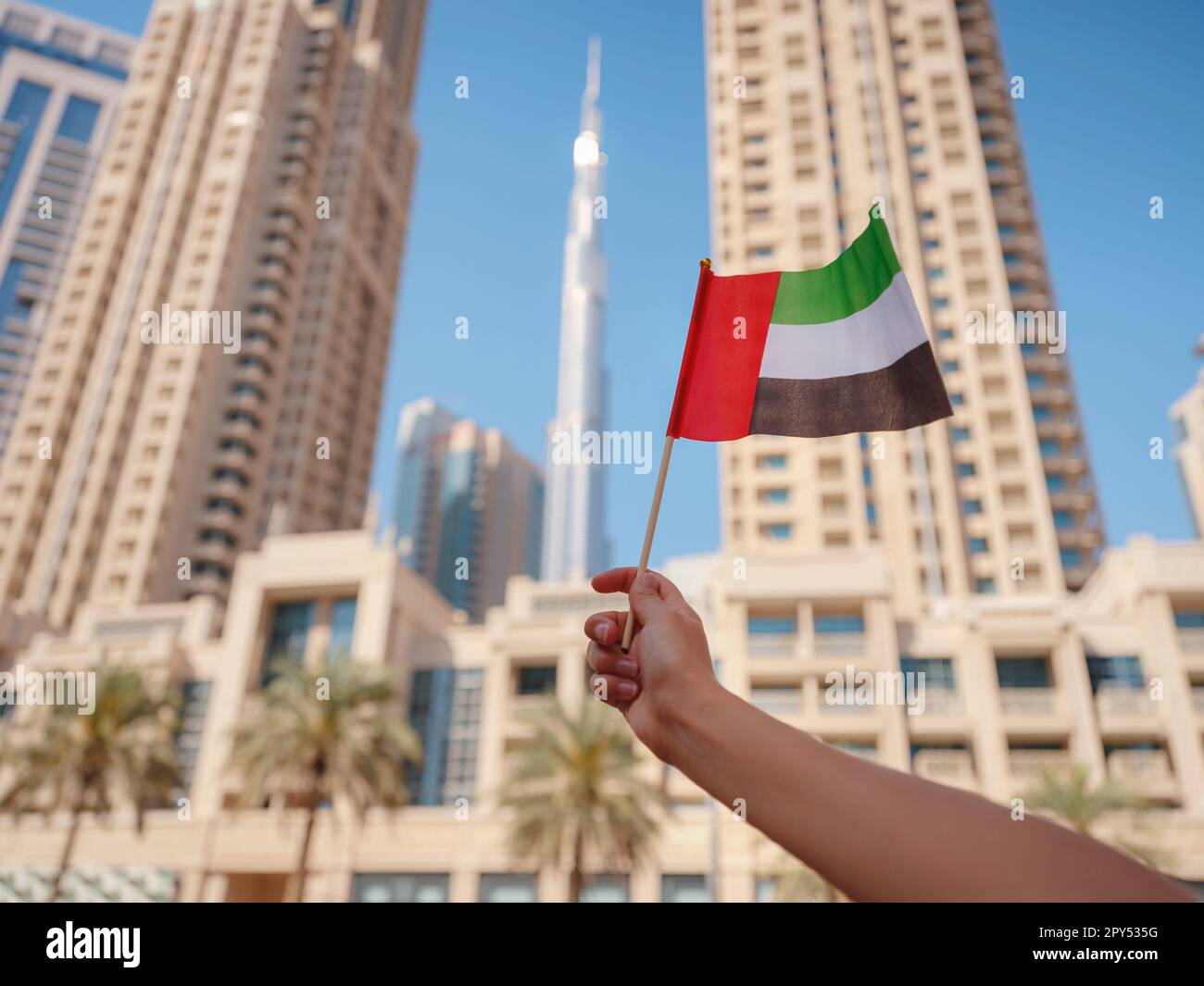 Close up of a female hand holding tiny flag of UAE against Dubai ...