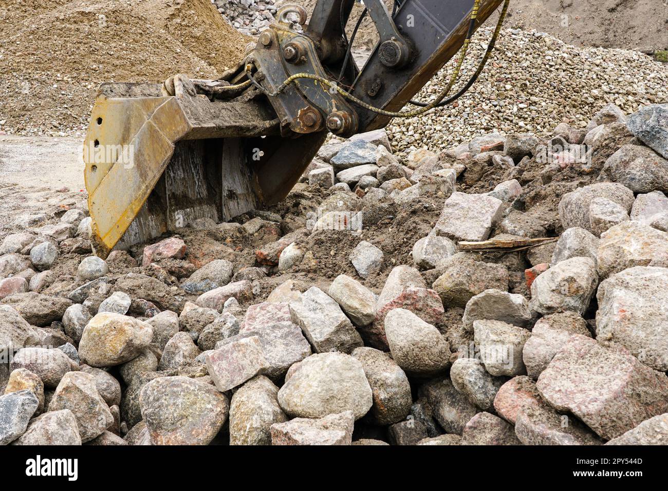 A bucket of a large hydraulic excavator rakes stones into a pile, an ...