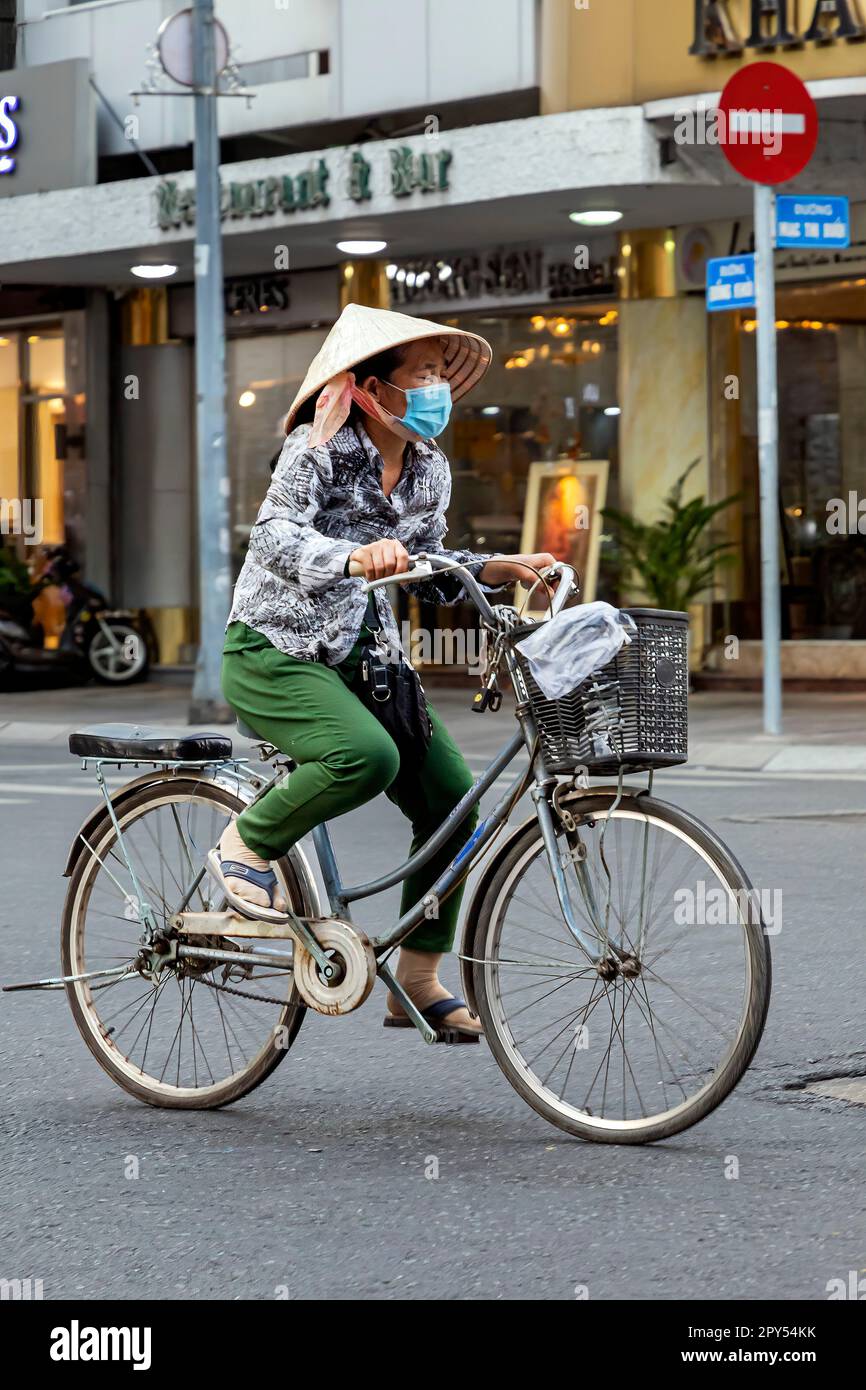 Vietnamese lady wearing bamboo hat riding bicycle through central Ho ...
