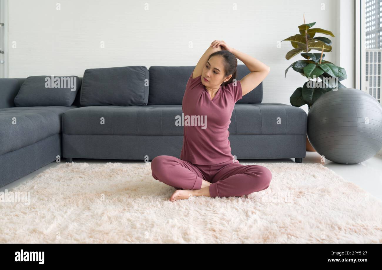Asian housewife stretching while sitting during home workout on carpet ...