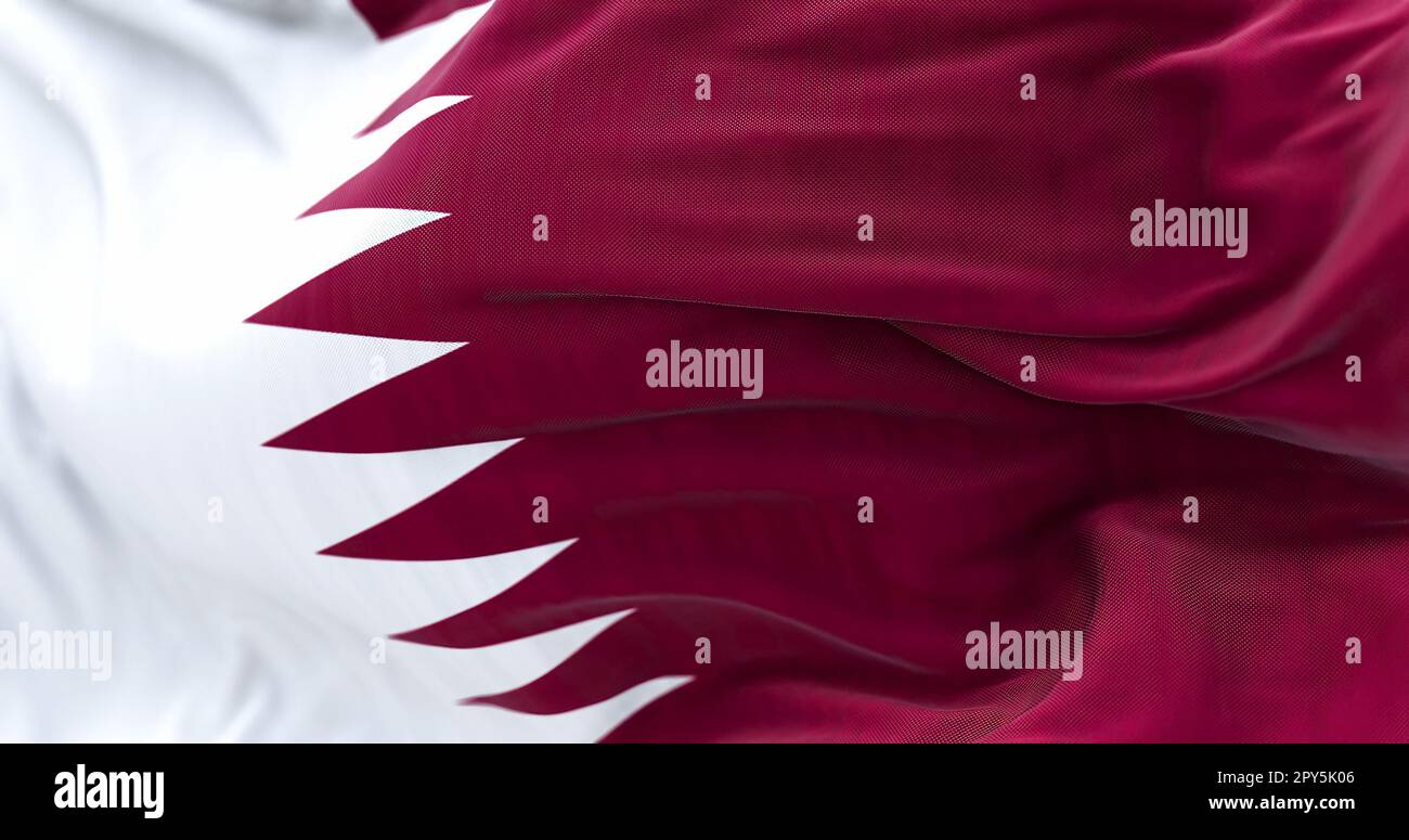 Detail of the Qatar national flag fluttering. The flag is maroon with a ...