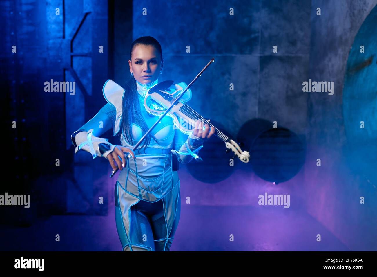 Young woman playing violin solo on stage illuminated with neon light ...