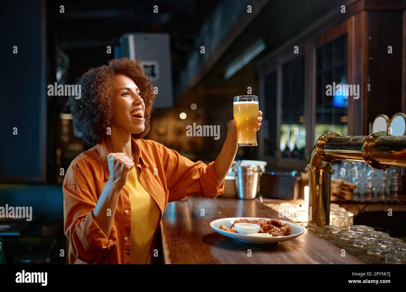 Young woman cheering for favorite team watching match in sports bar ...