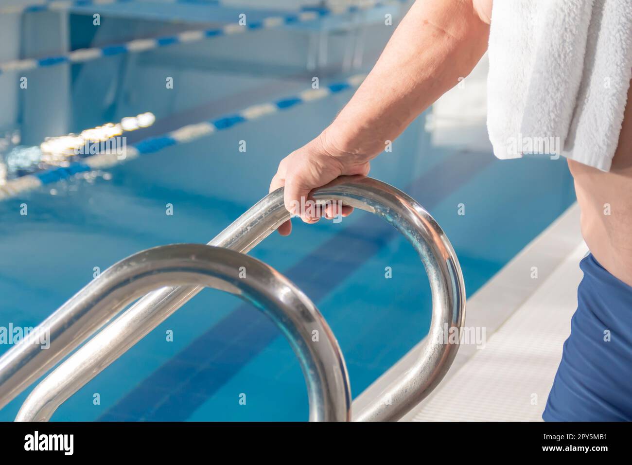 An elderly man stands near the descent into a pool of clear, blue water ...