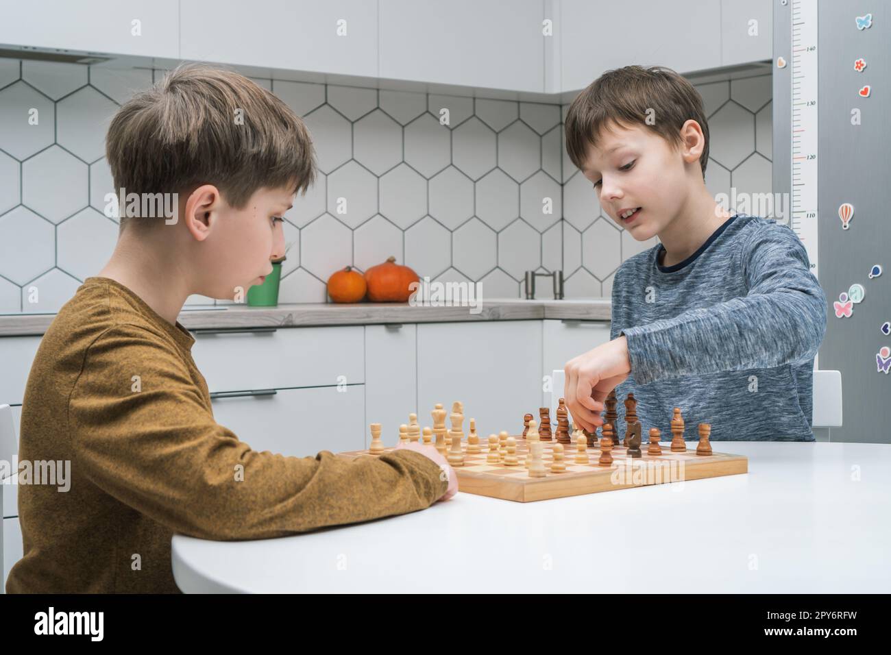 Schoolboys play chess on kitchen table, side view. Chessboard with ...