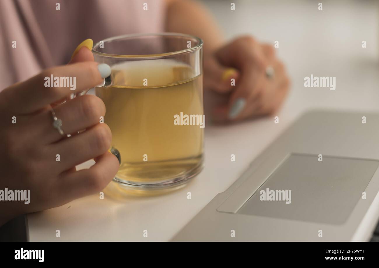 Female hands holding hot cup of tea close-up with laptop background ...