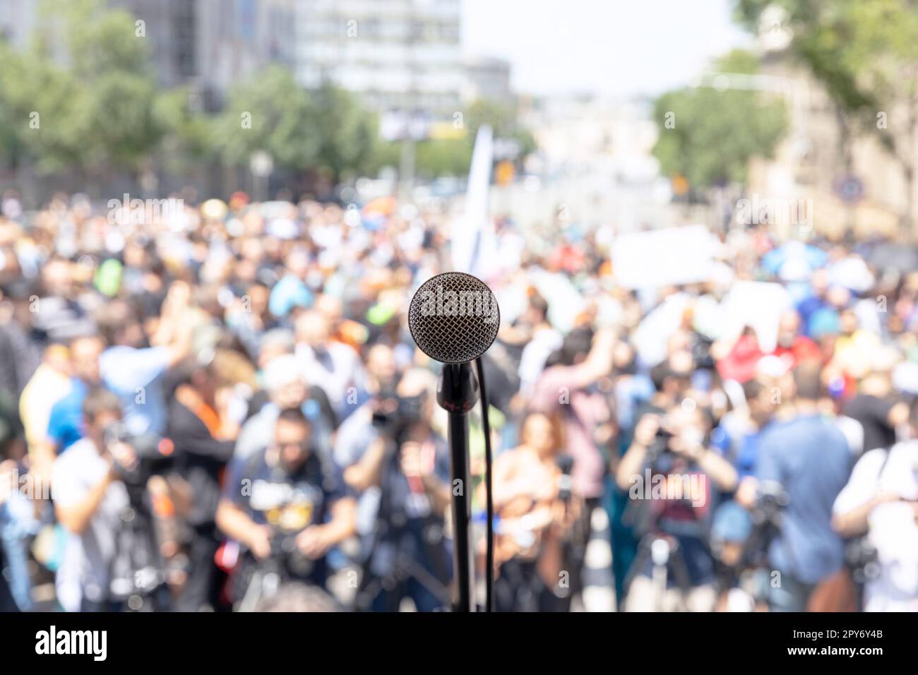 Focus on microphone, blurred group of people at mass protest in the ...