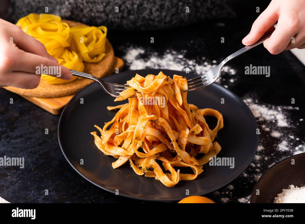 A close-up of hands holding a fork, digging into a plate of fast food ...