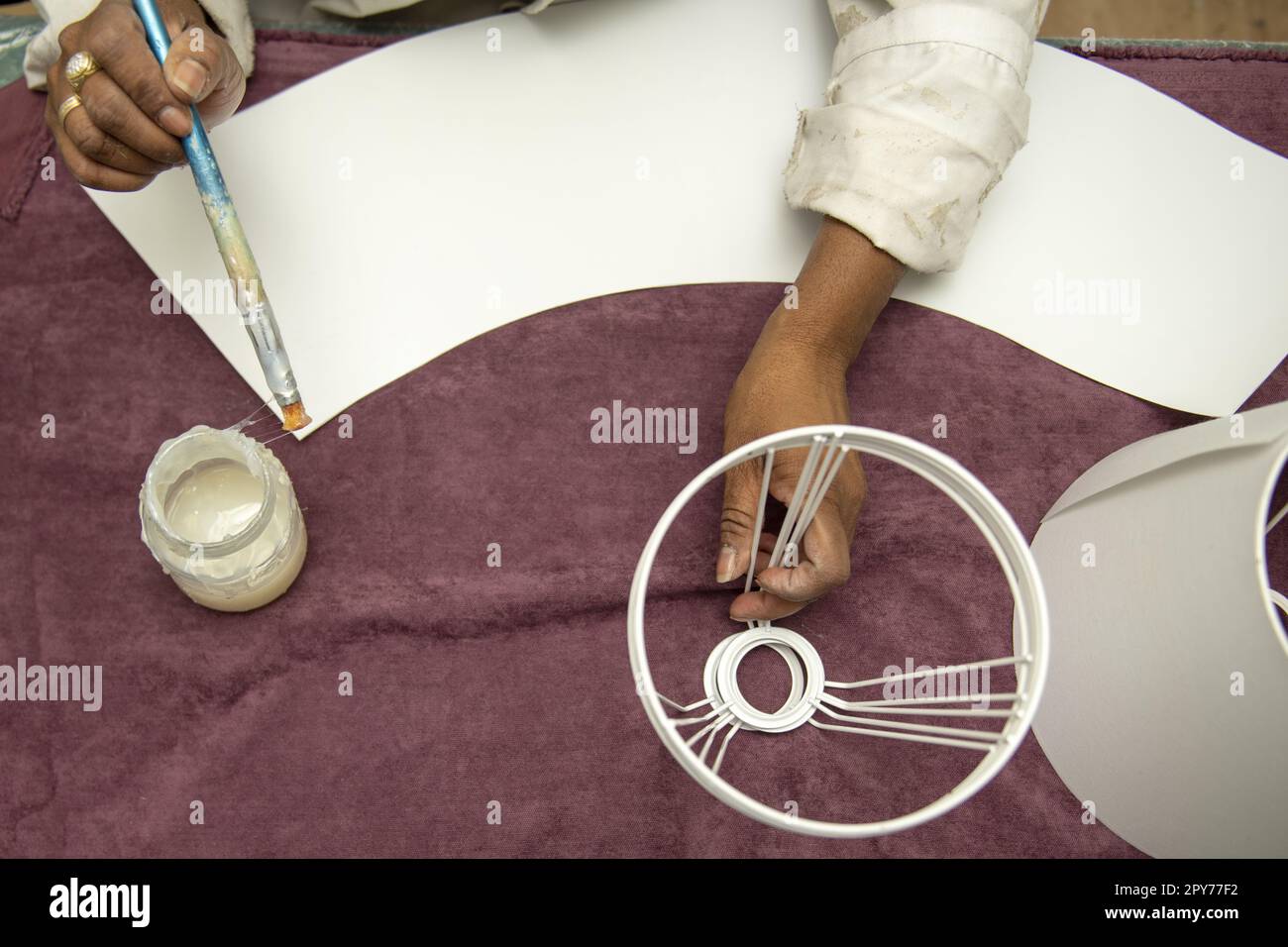 The brown hands of a lady making a lamp with frames and glue to glue ...