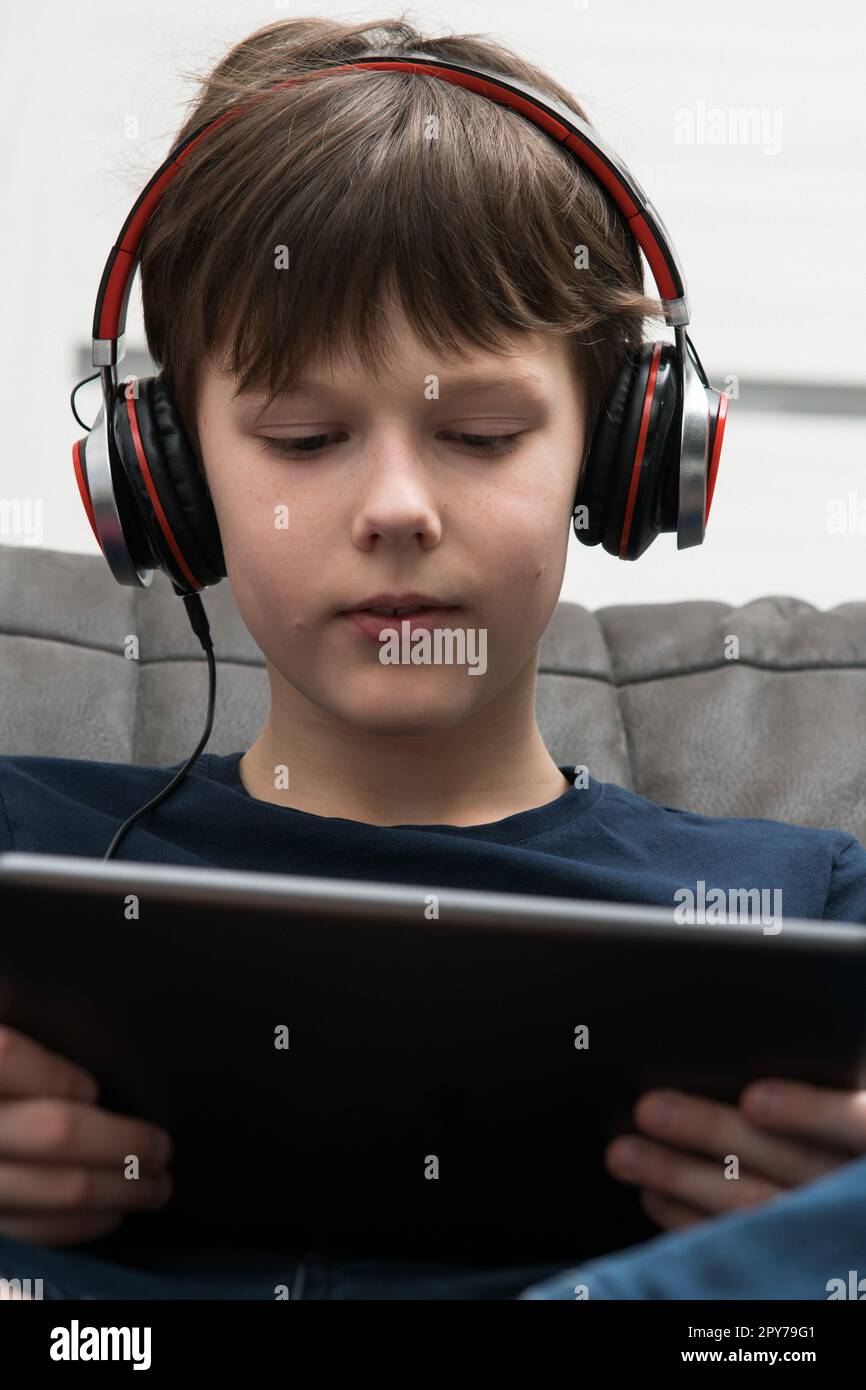 Smiling, brunette little boy in wired headphones watch movies, listen ...