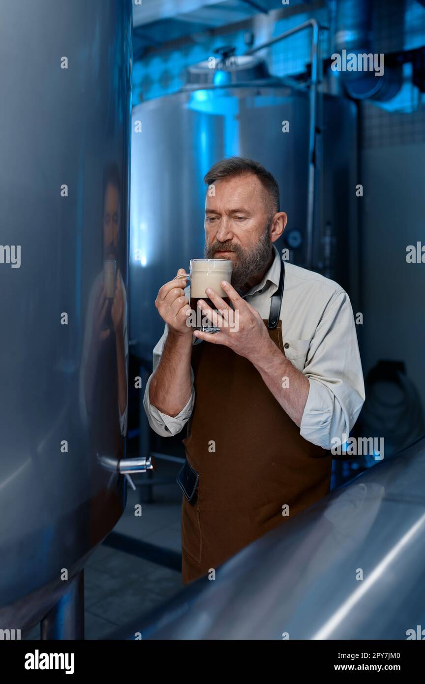 Brewer tasting fresh brewed beer while standing in front of metal ...