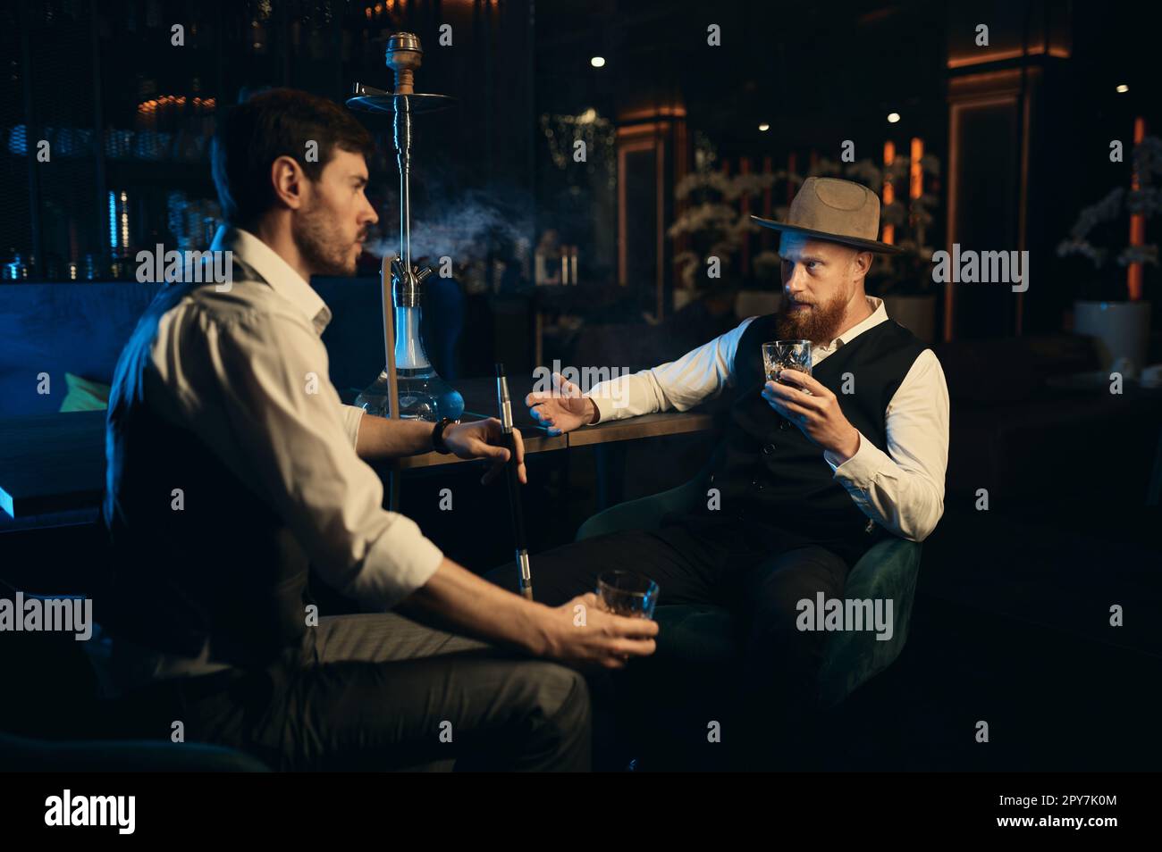Guys having serious conversation while sitting face to face at hookah ...
