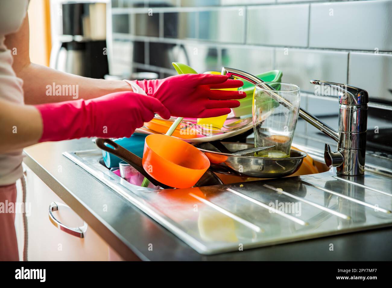Kitchen sink full of dirty dishes. Woman in pink rubber gloves doing ...