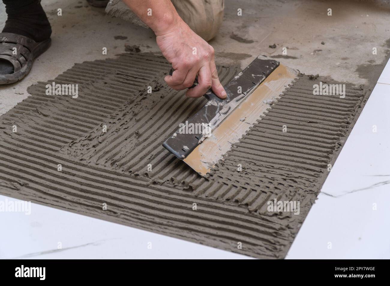 A construction worker applies cement for laying floor ceramic tiles ...