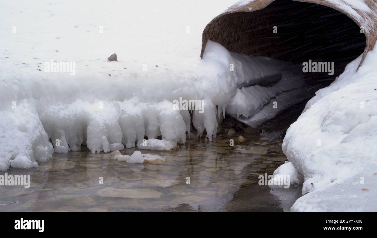 A rusty sewer pipe drains sewage and polluted water into a frozen river ...