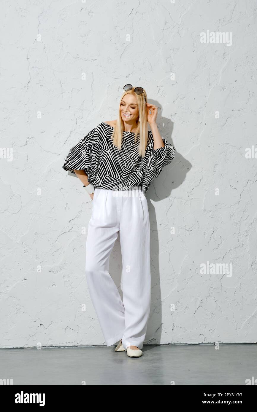 Cheerful and positive woman in striped blouse and wide trousers leaning ...
