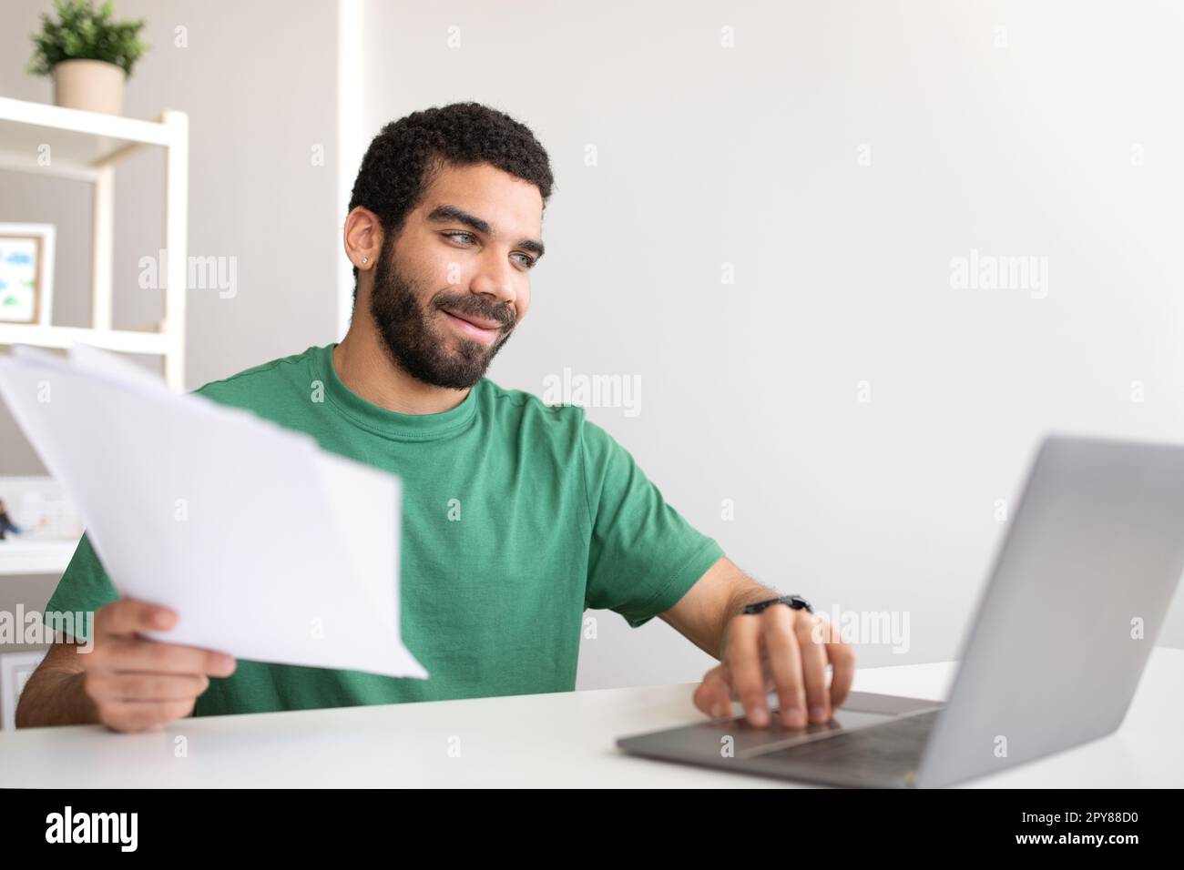 Smiling young middle eastern guy blogger at workplace with laptop works ...