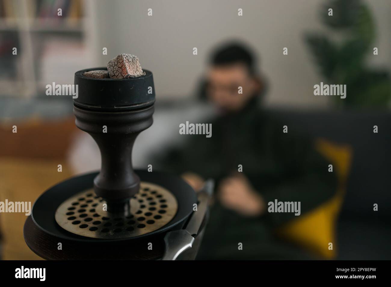 Hookah shisha with glass flask and metal bowl in room with man ...