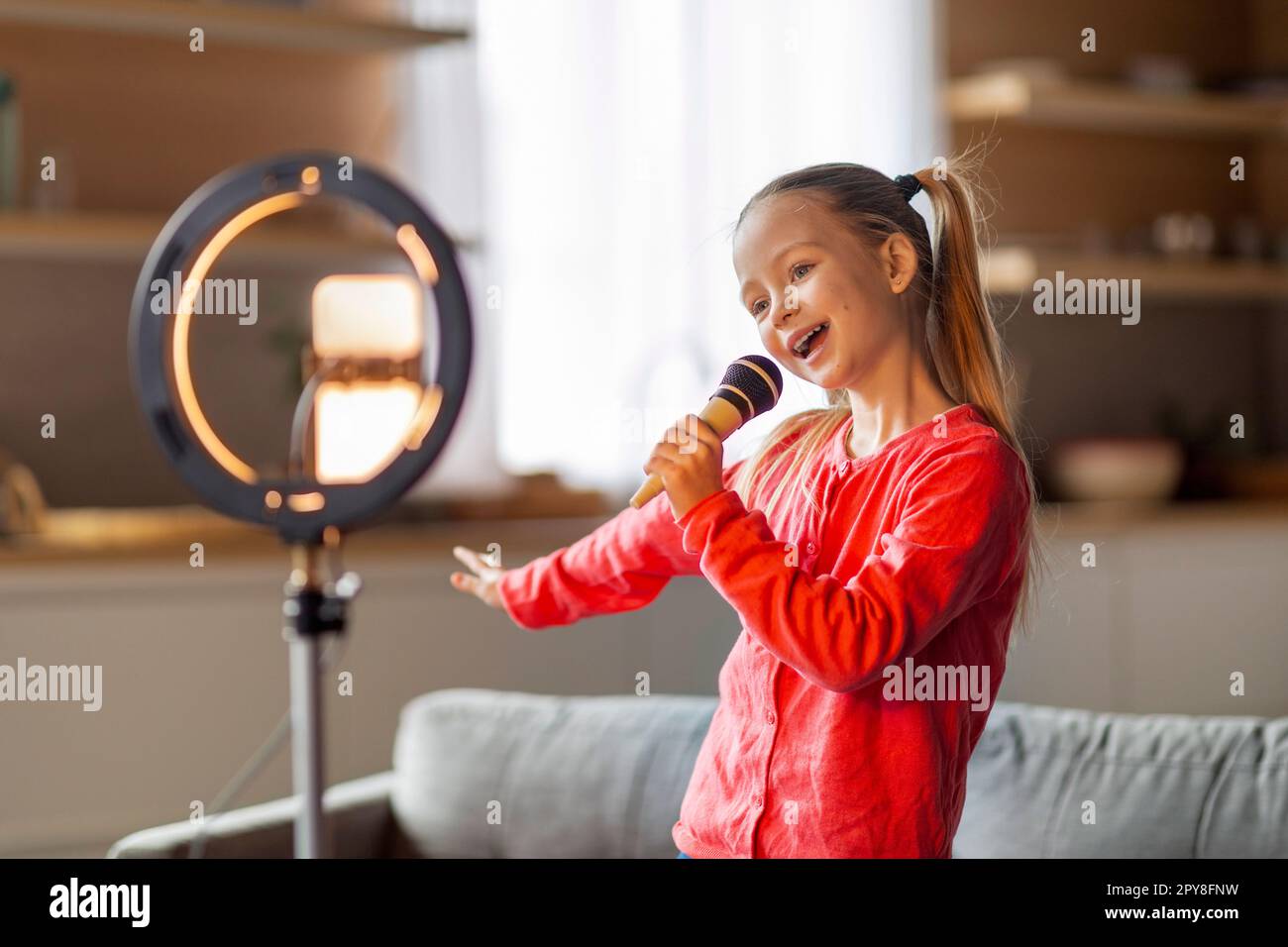 Happy cute little girl singing and dancing while recording video at ...