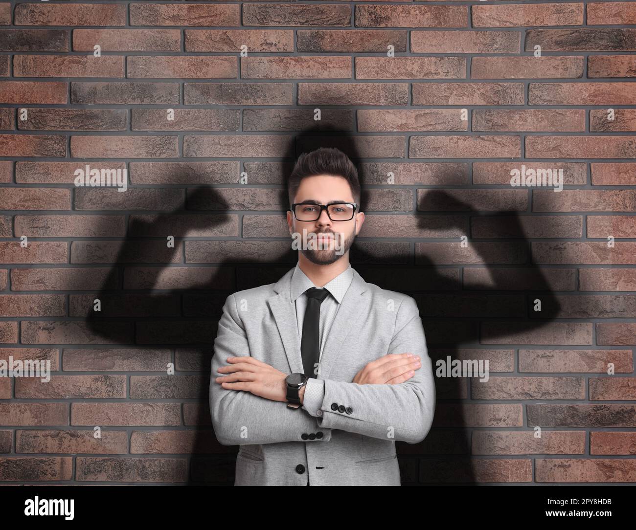 Businessman and shadow of strong muscular man behind him on brick wall ...