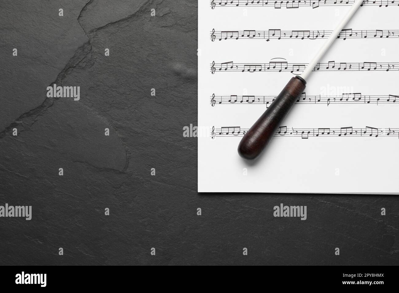 Conductor's baton and sheet music on black background, top view. Space ...