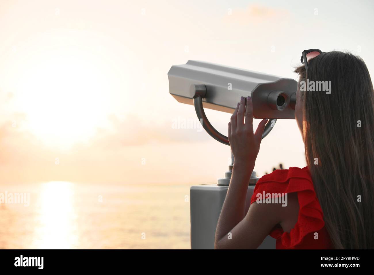 Young woman looking through tourist viewing machine at observation deck ...