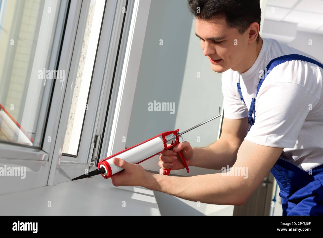 Worker sealing plastic window with caulk indoors. Installation process ...