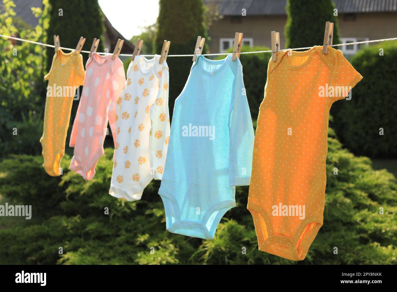 Clean baby onesies hanging on washing line in garden. Drying clothes ...