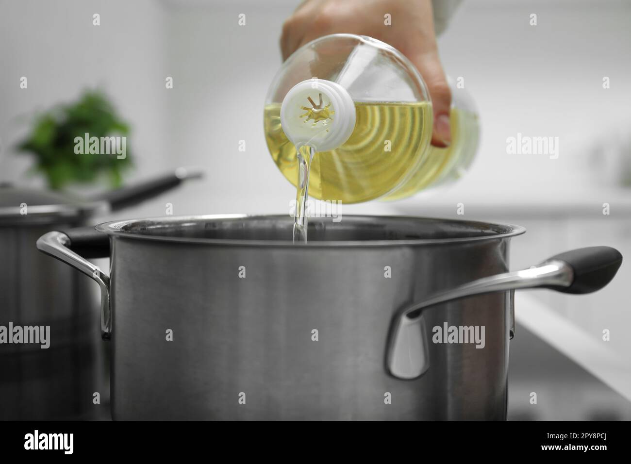 Woman pouring cooking oil from bottle into pot in kitchen, closeup ...