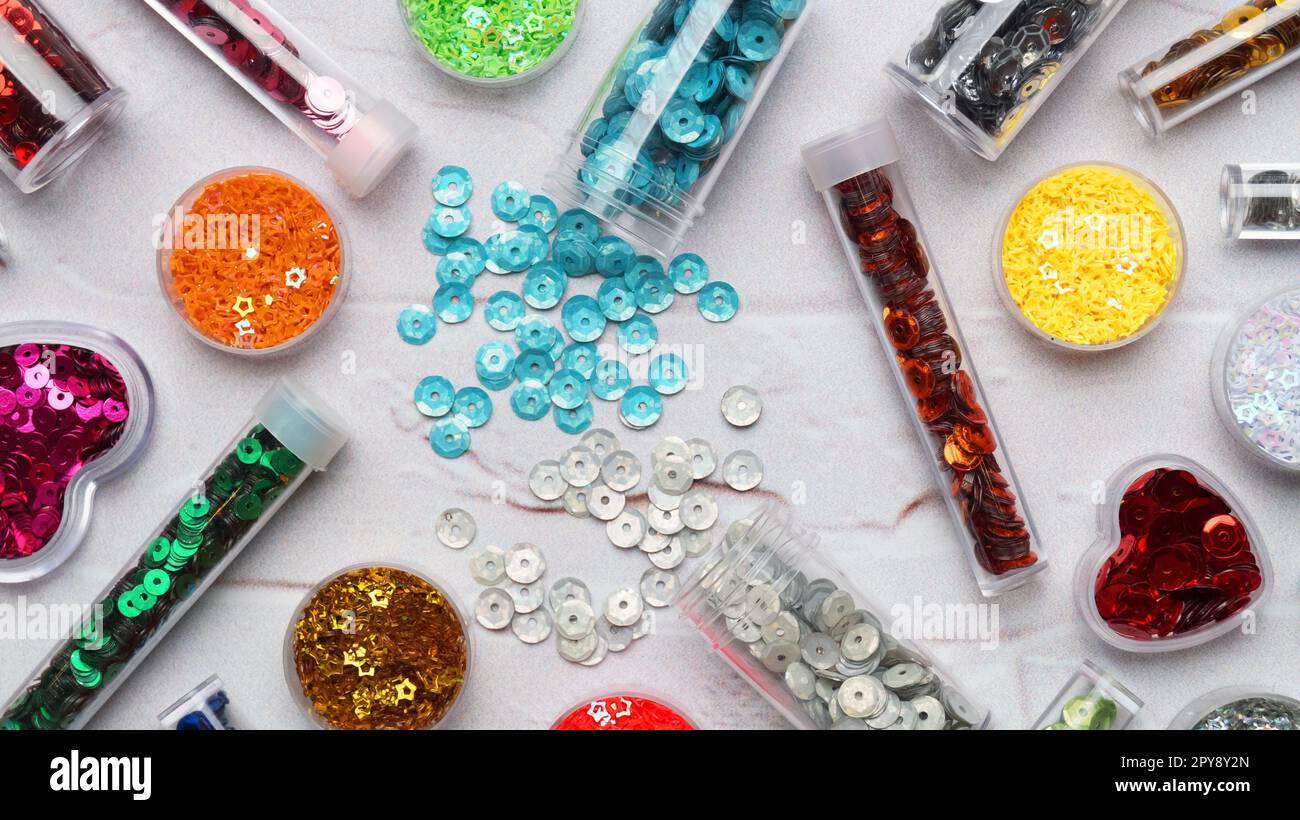 Many different colorful sequins in containers and tubes on marble e ...