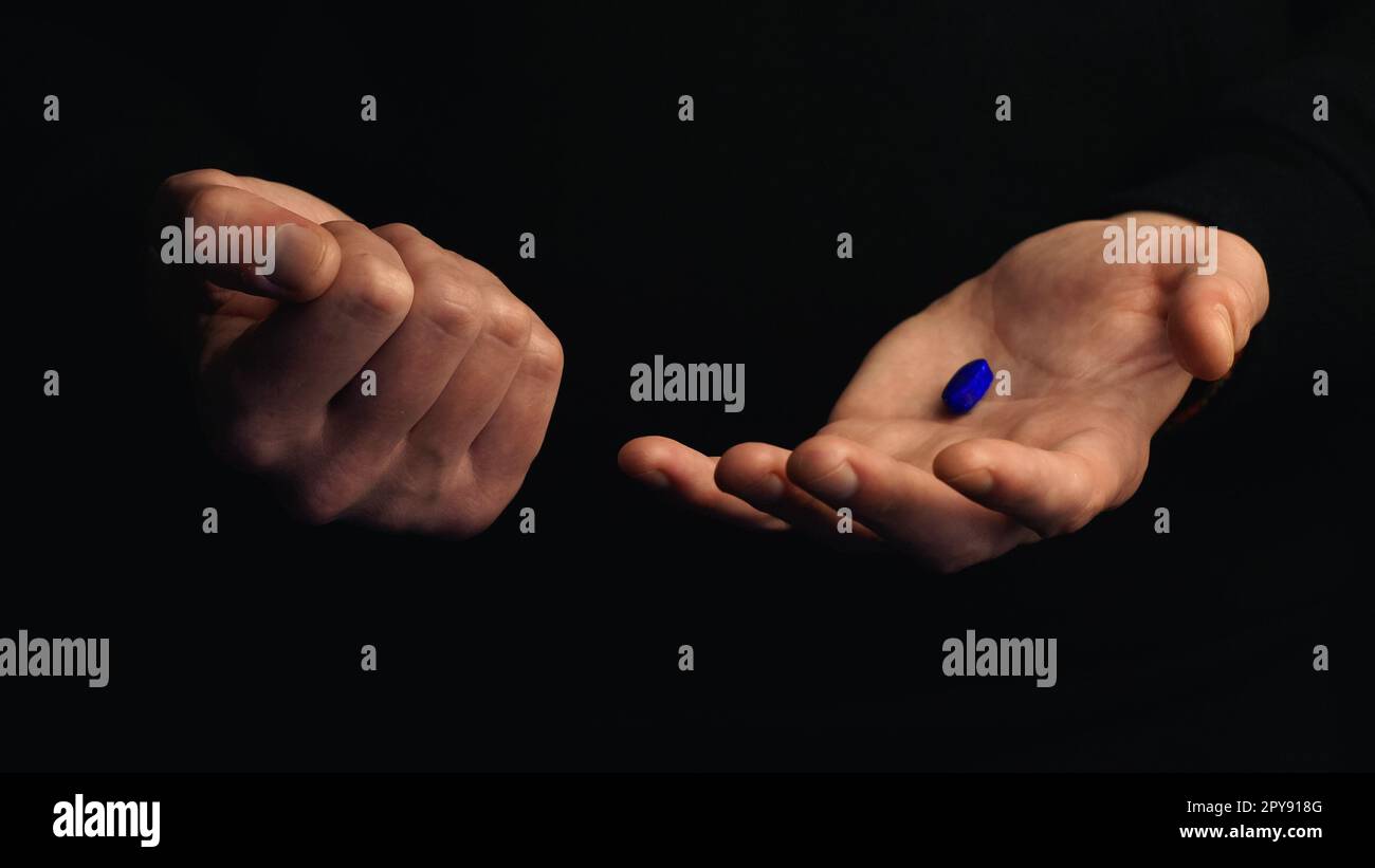 Studio shot male hands show blue pill isolated on black background ...