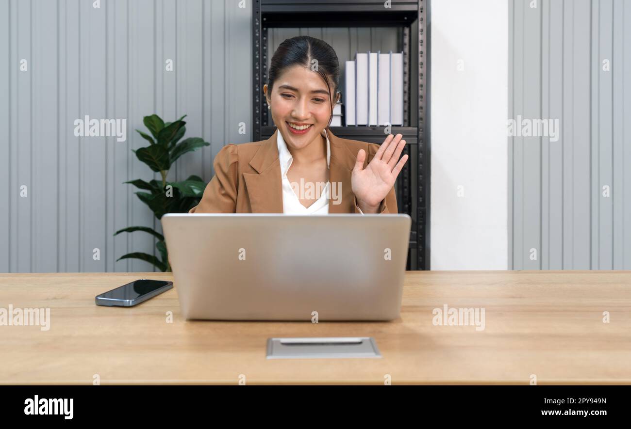 Young asian female employee in a brown suit waving hand on laptop ...