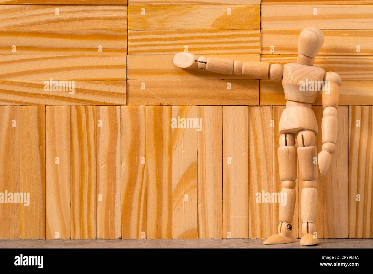 Wooden man figure staying next to wooden wall made fromwooden blocks ...