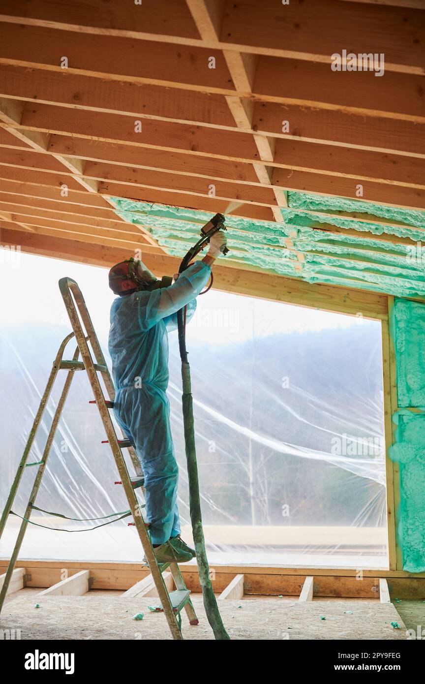 Male builder insulating wooden frame house. Man worker spraying ...