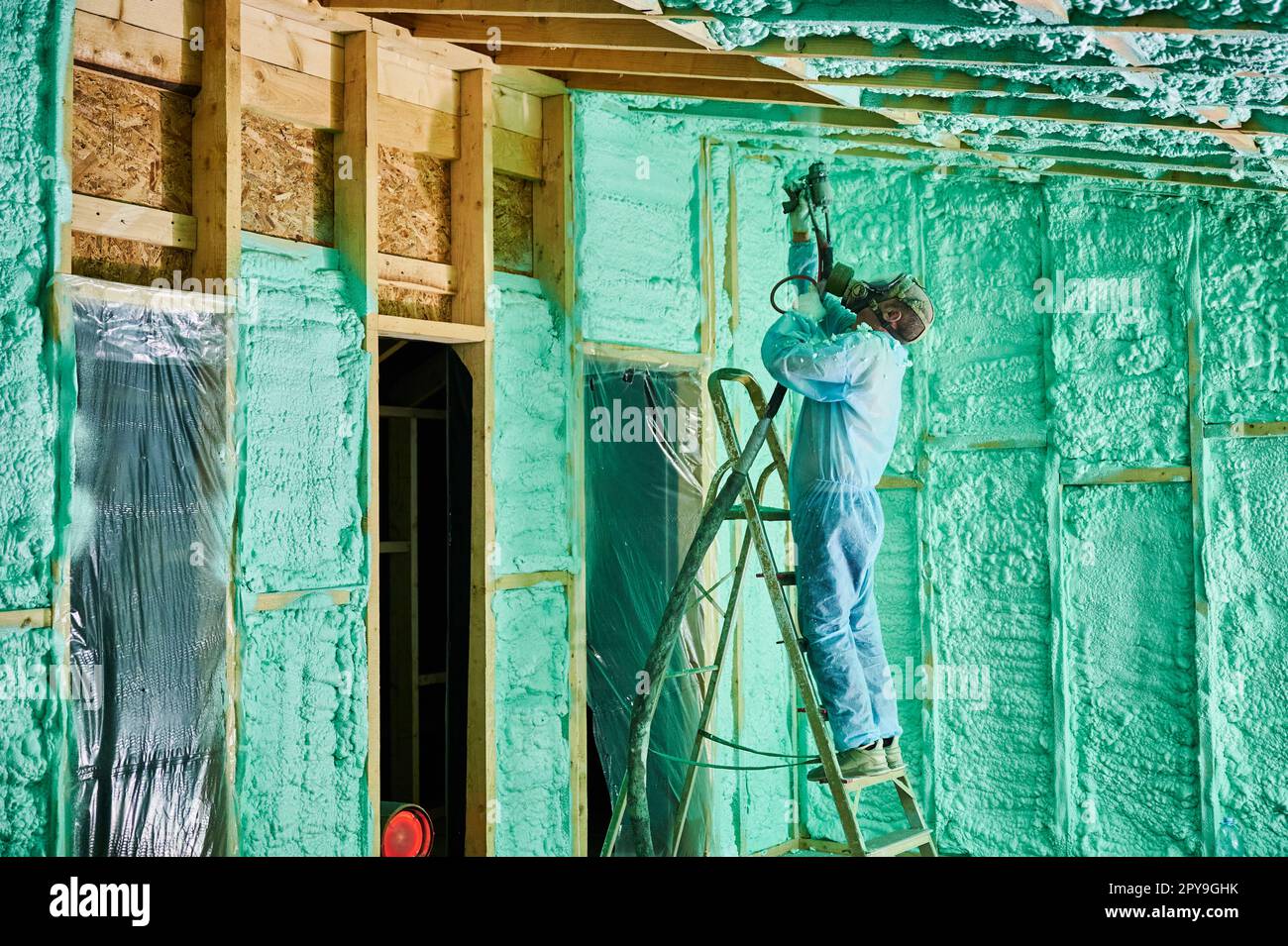 Male builder insulating wooden frame house. Man worker spraying ...