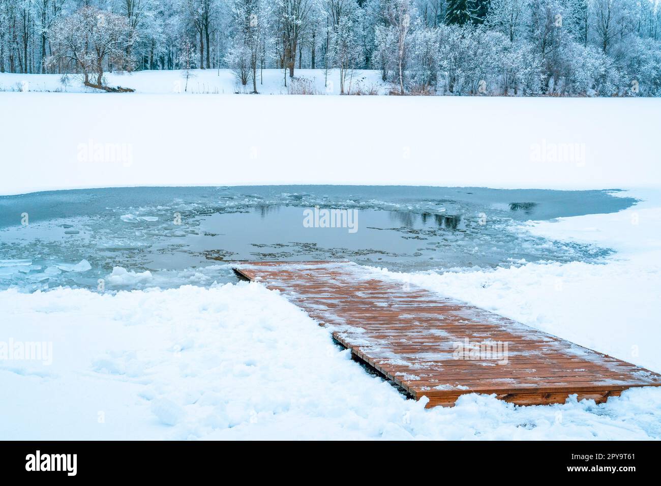 An ice hole on a frozen lake with a snow-covered wooden path descending ...