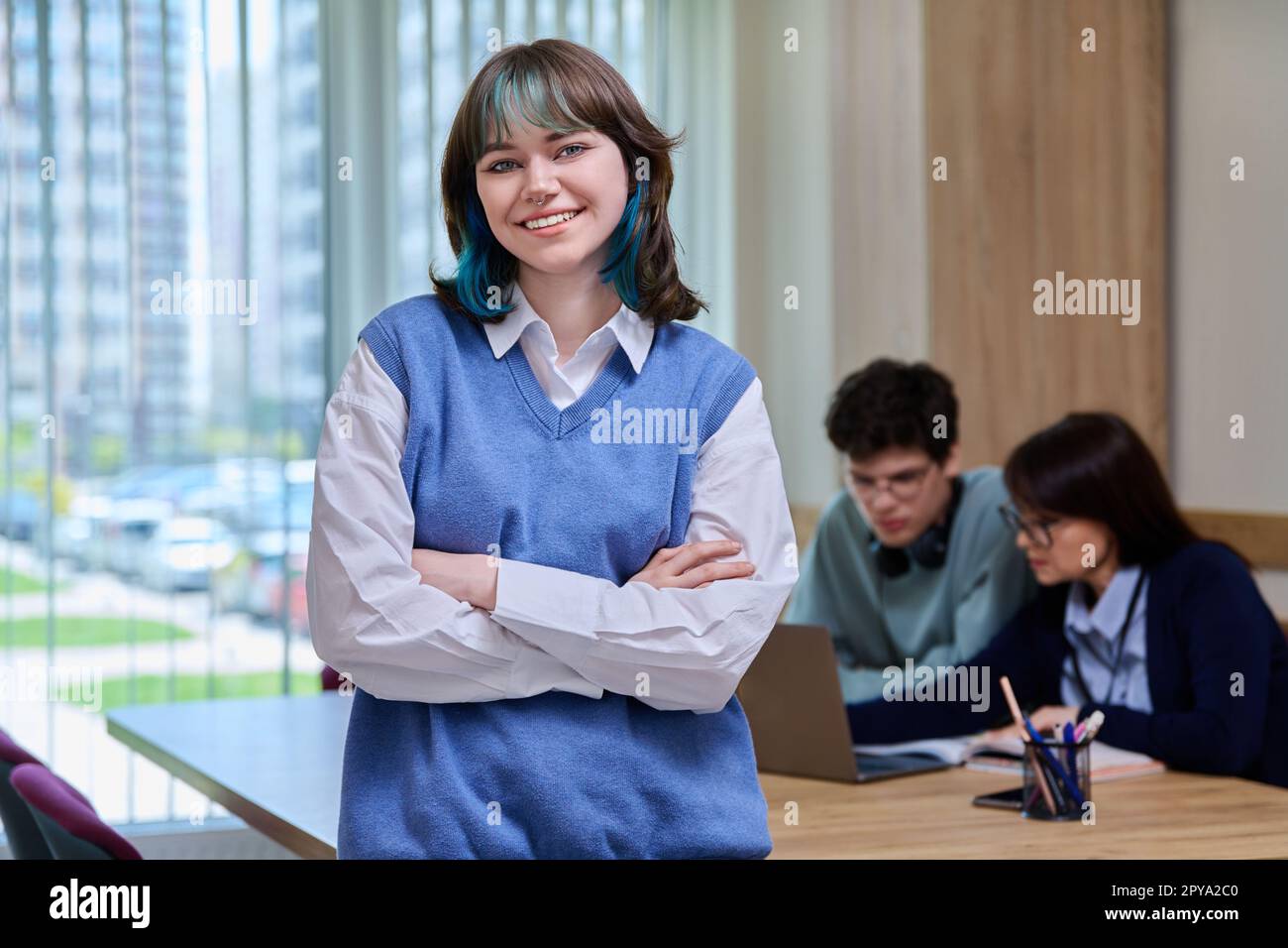 Smiling trendy female student looking at camera, posing in college ...