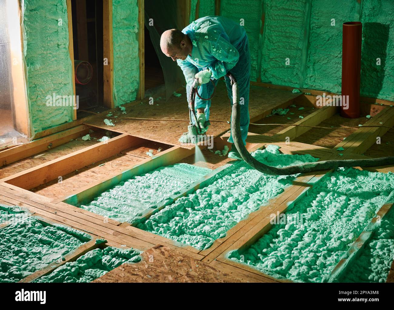Male builder insulating wooden frame house. Man worker spraying ...