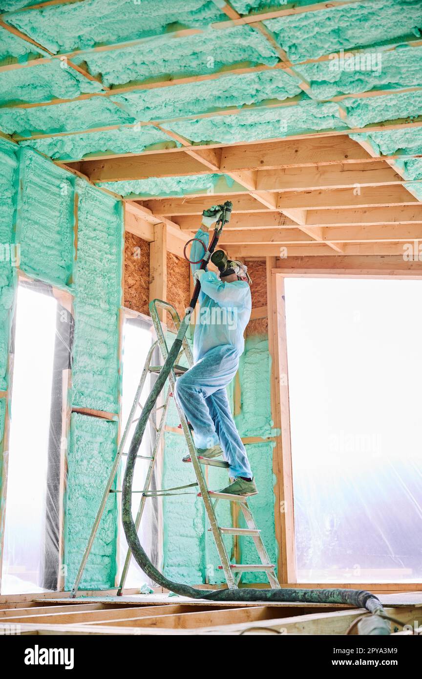 Male builder insulating wooden frame house. Man worker spraying ...
