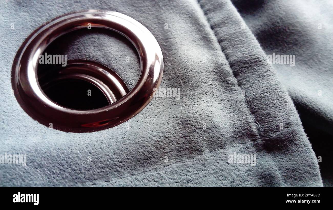 close-up of a metal eyelet on a gray-blue curtain made of thick velvety ...