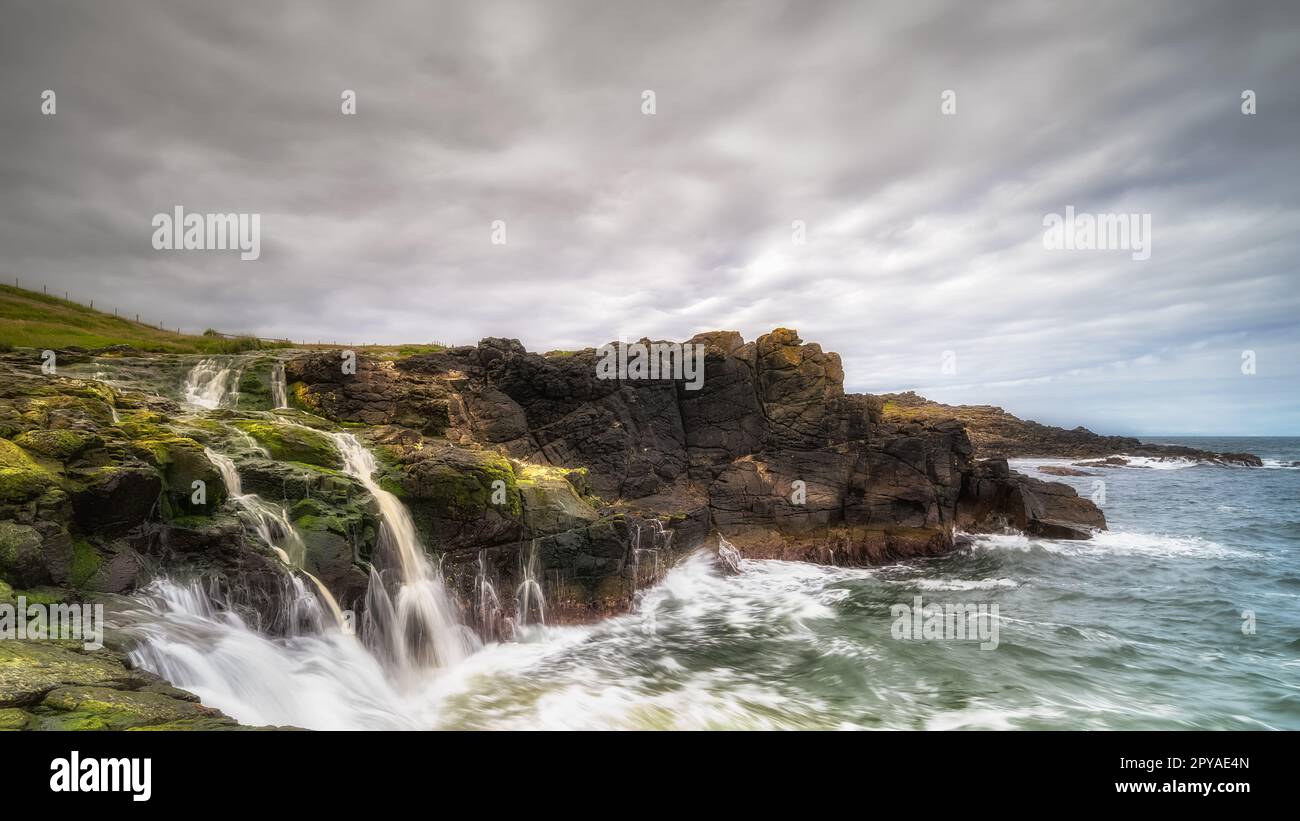 Dunseverick Falls with small cliffs and streaks of water falling down ...