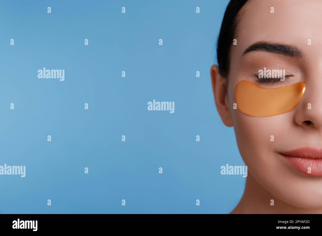 Beautiful young woman with under eye patch on light blue background ...