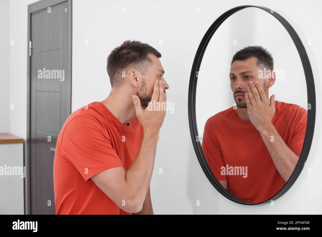 Sleep deprived man looking at himself in mirror indoors Stock Photo - Alamy