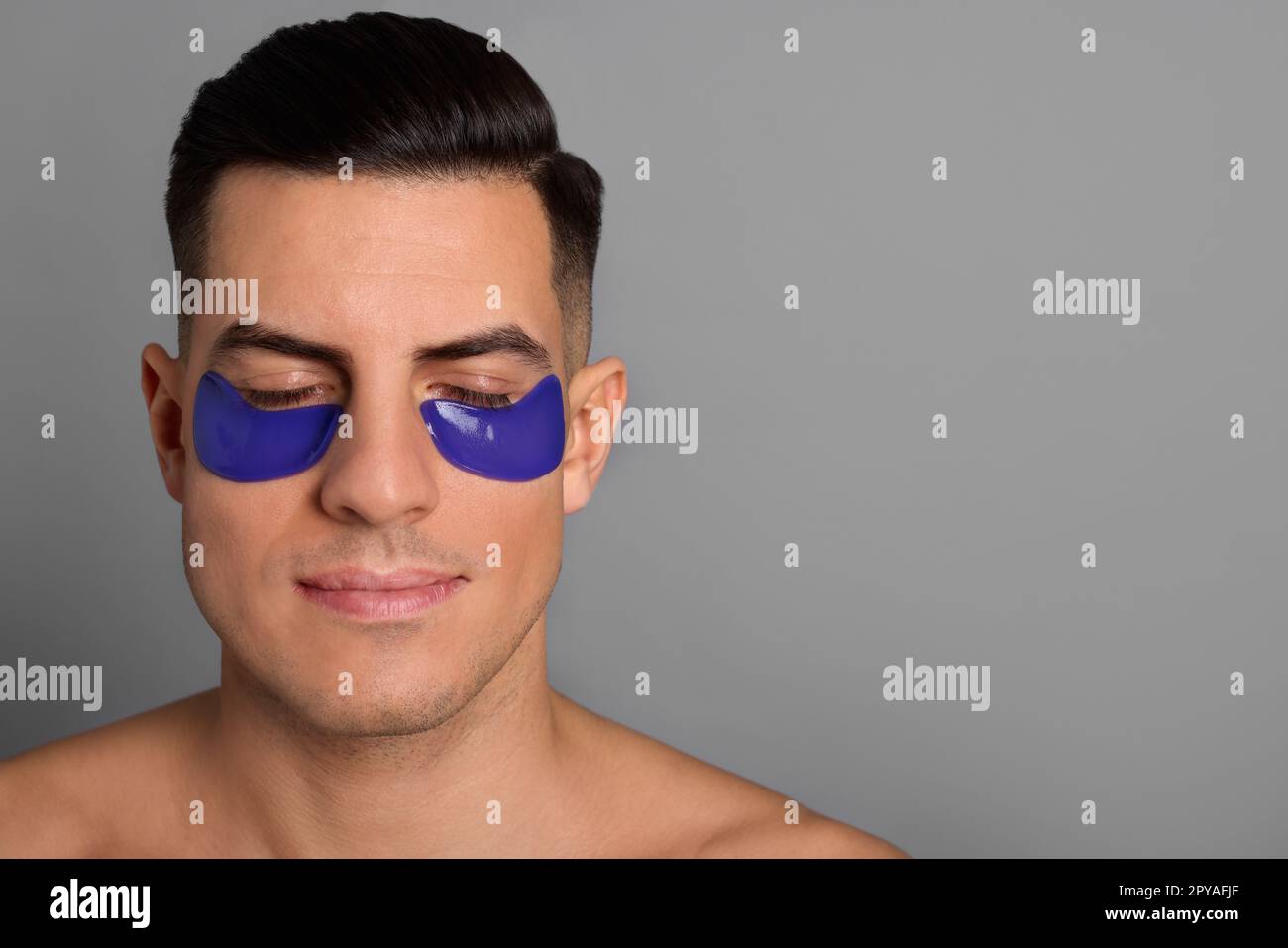 Man with blue under eye patches on grey background. Space for text ...