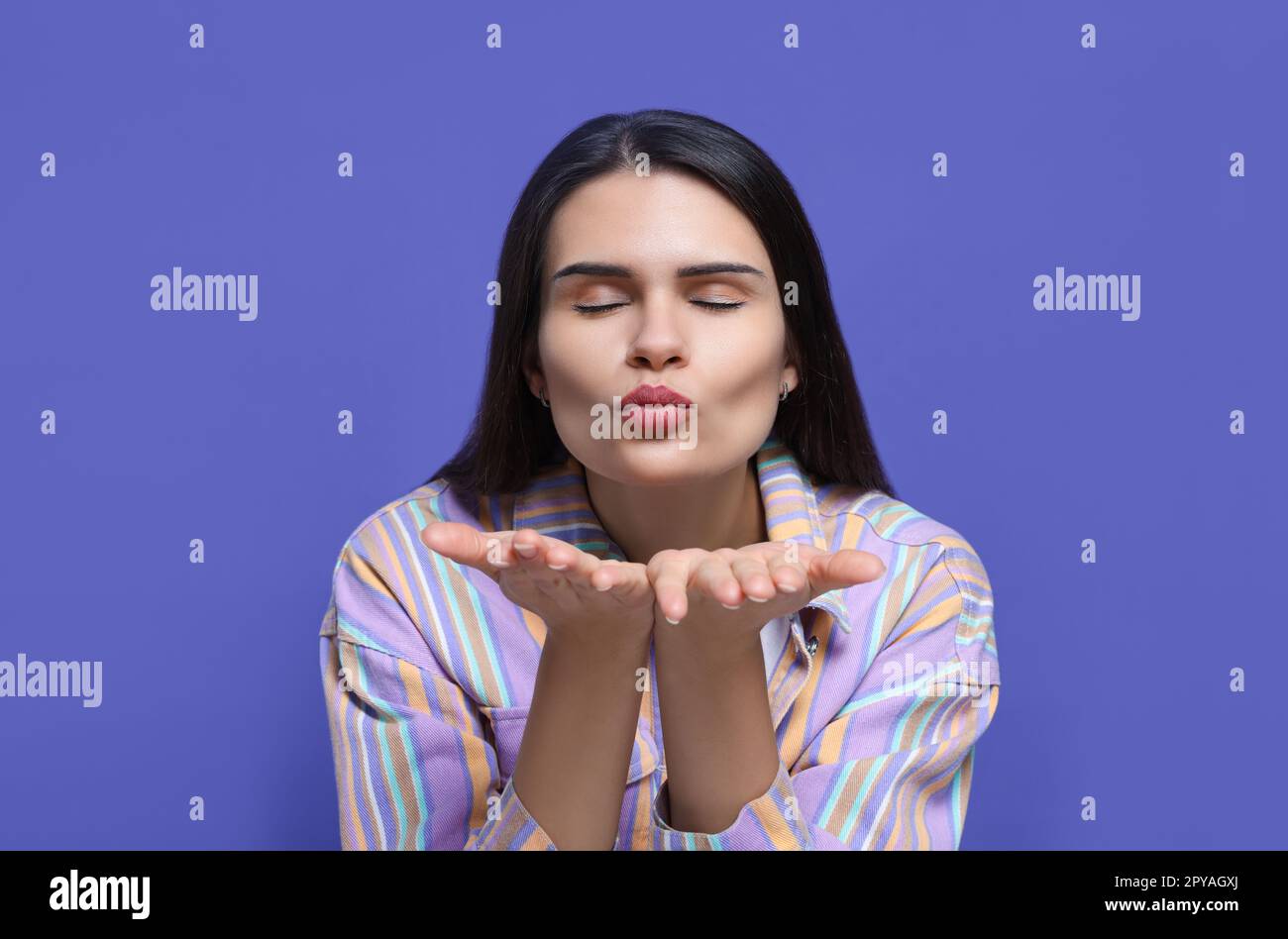 Beautiful young woman blowing kiss on purple background Stock Photo - Alamy