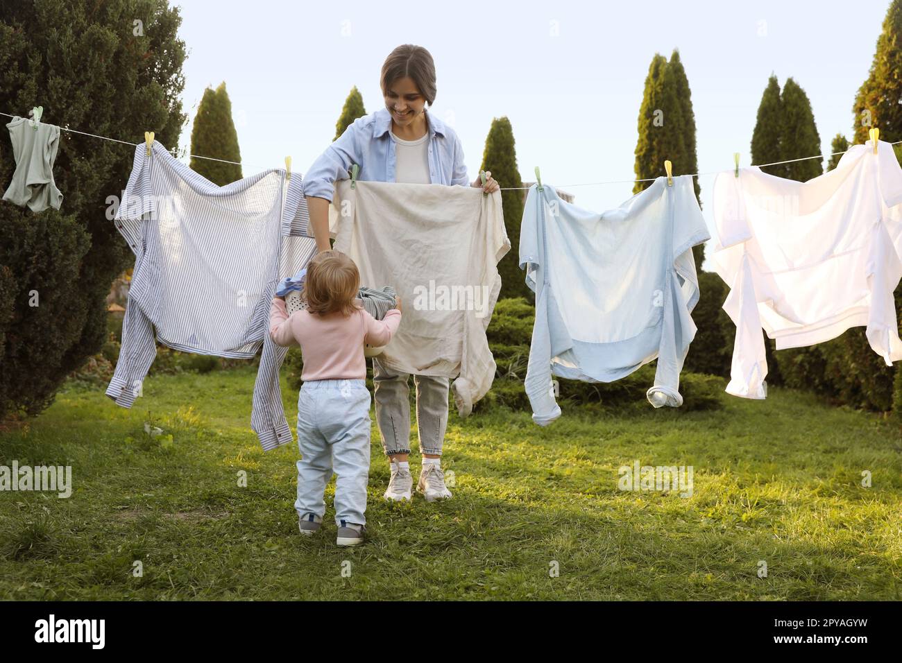 Mother and daughter hanging clothes with clothespins on washing line ...