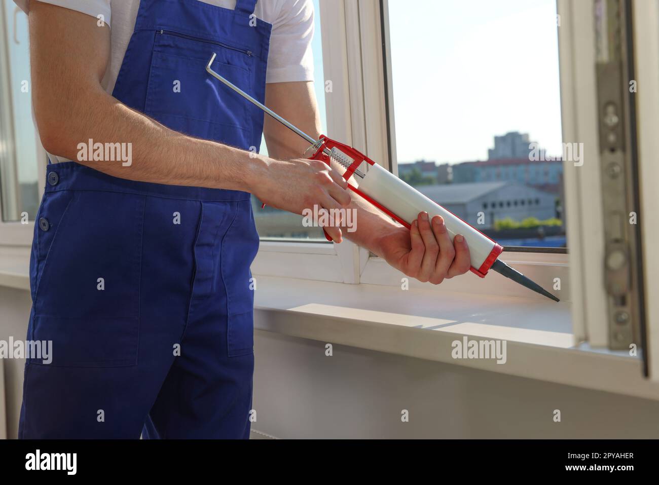 Worker sealing plastic window with caulk indoors, closeup. Installation ...