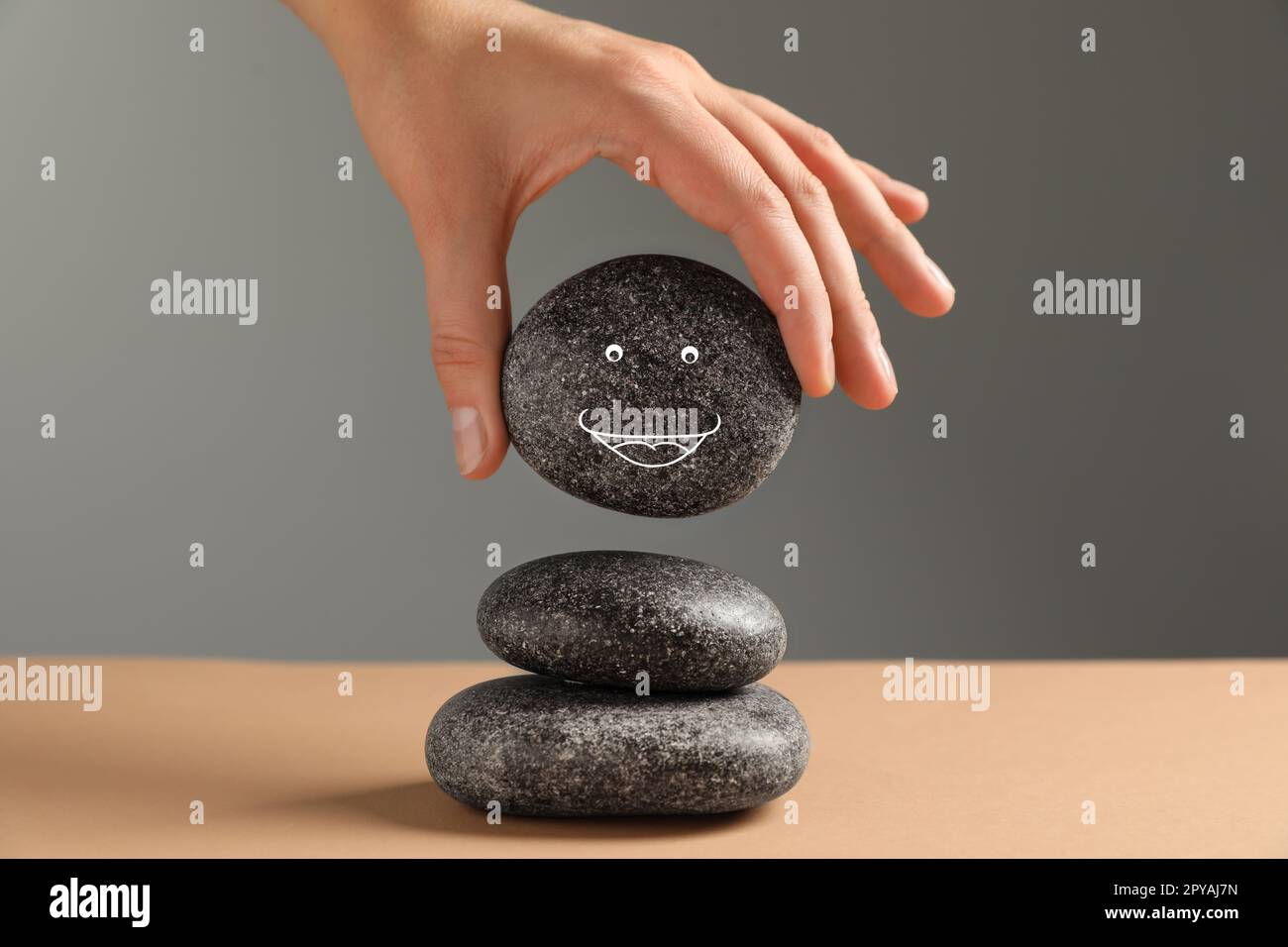 Woman putting stone with drawn happy face on stack against grey ...