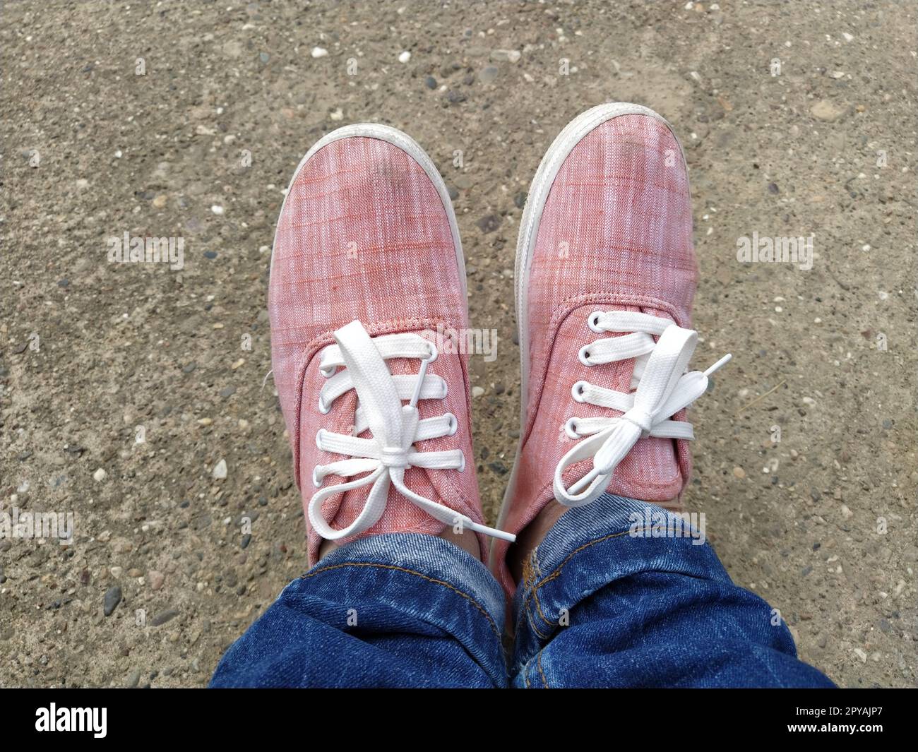 Pink sneakers with white laces on the legs. Blue jeans wrapped ...