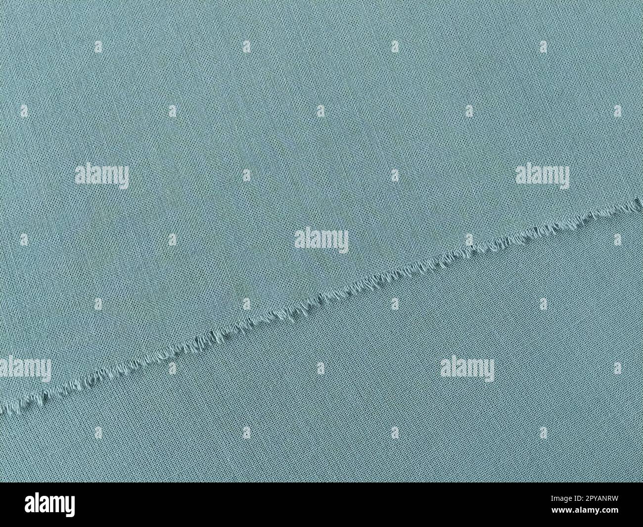 Ripped edge of fine woolen fabric in green or blue. Loose threads at ...